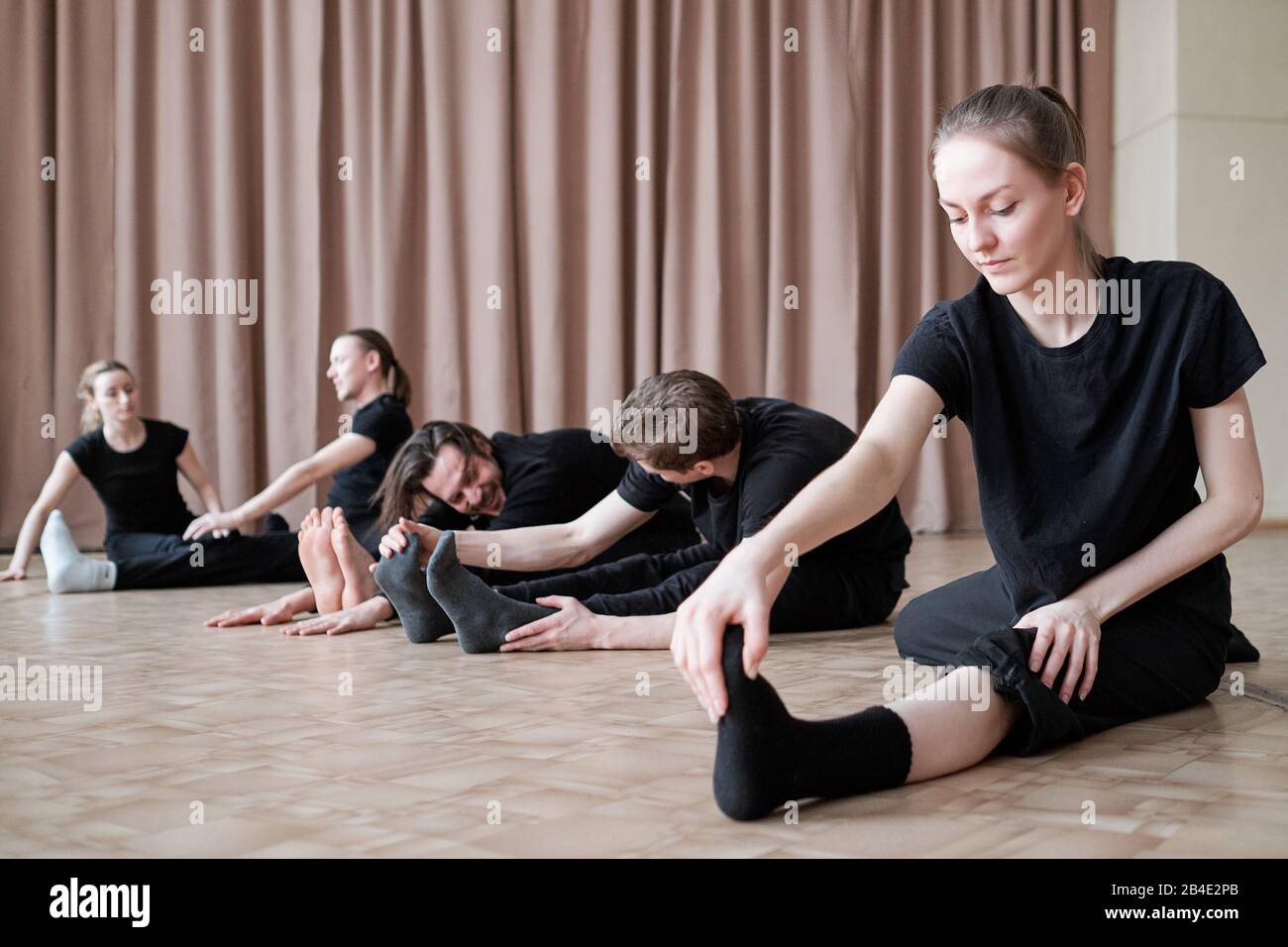Fit young female dancer stretching one leg while sitting on the floor ...