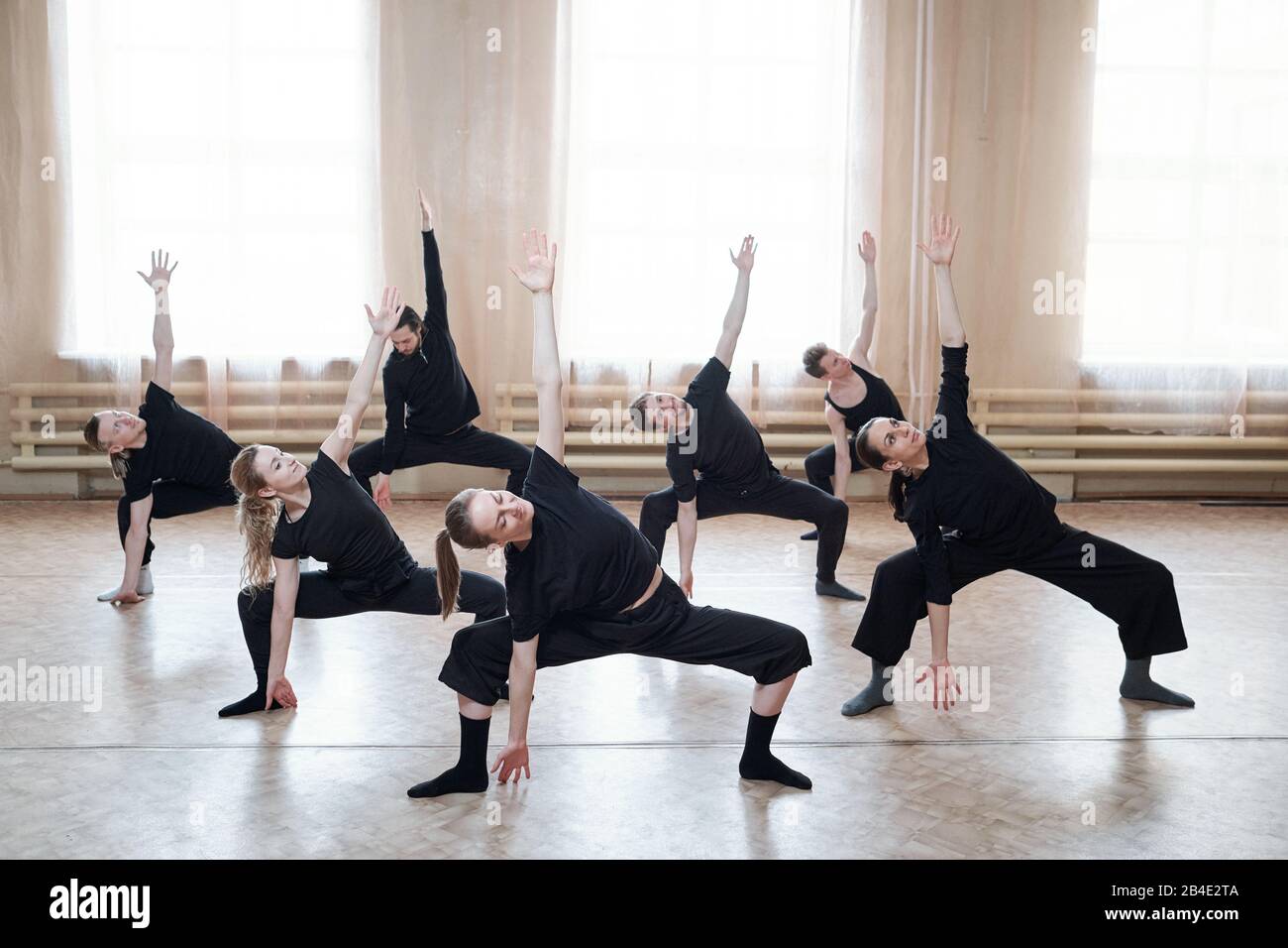 Large group of young fit people in black activewear exercising together ...