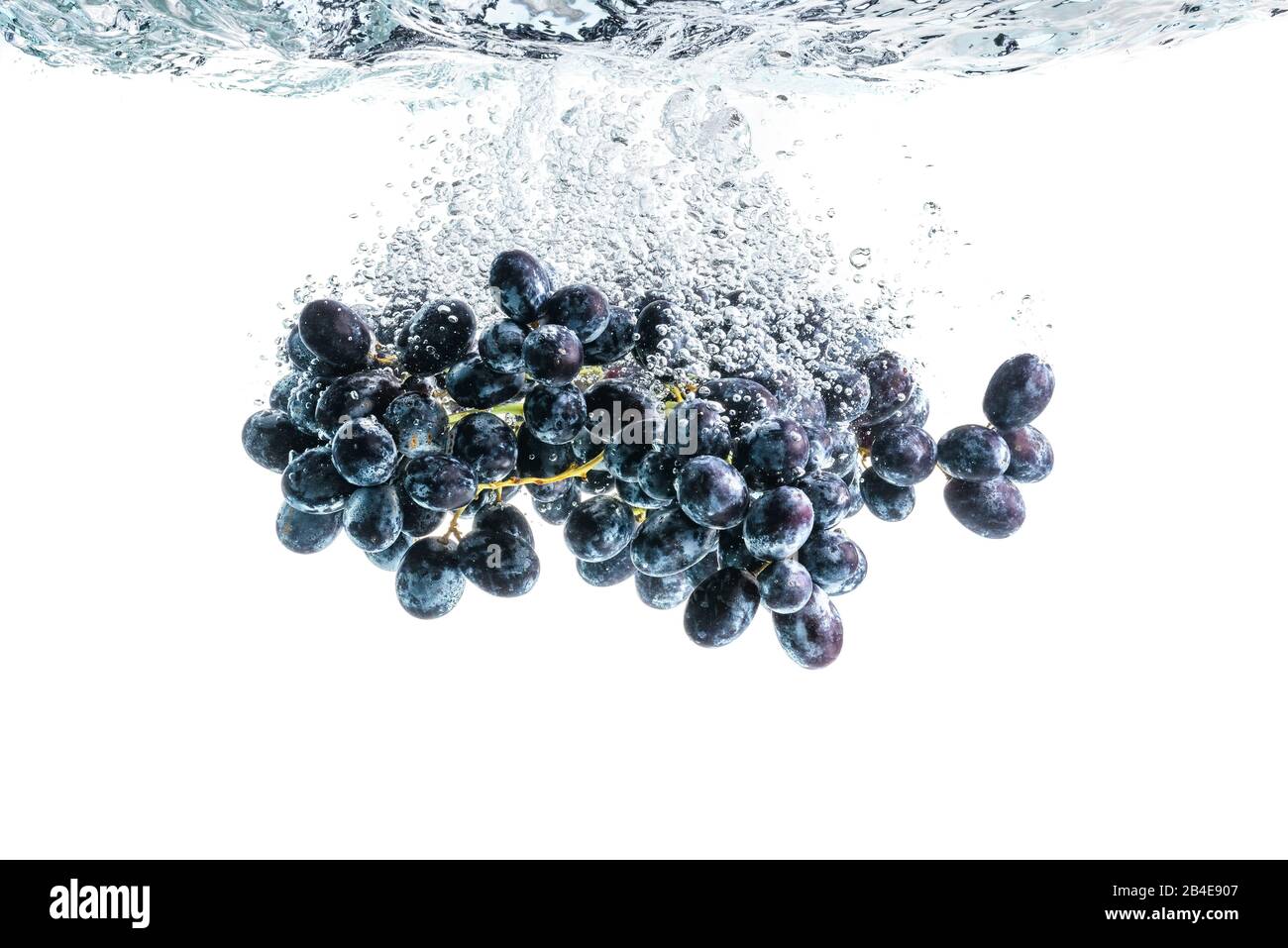 Bunch of red grapes splashing into crystal clear water on withe ...