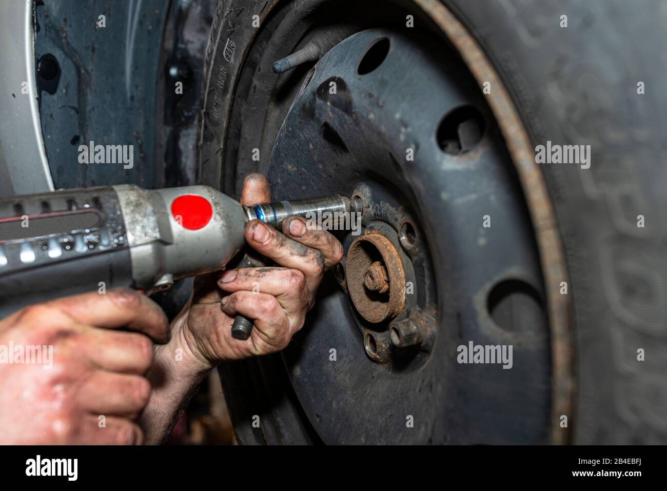 The car mechanic bolts the steel car wheel with a pneumatic wrench in a ...