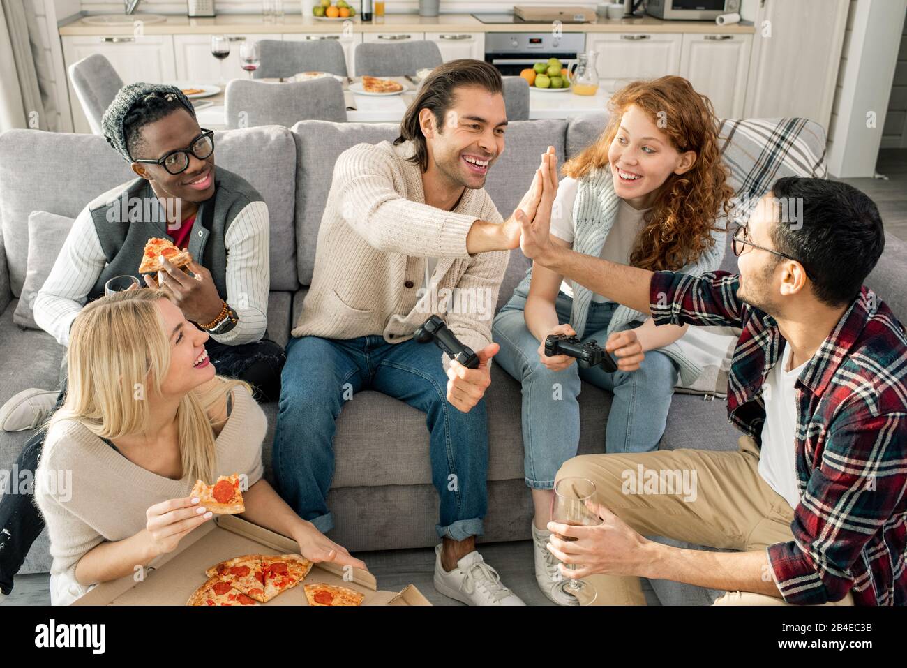 Two happy young men giving each other high five while sitting on couch ...