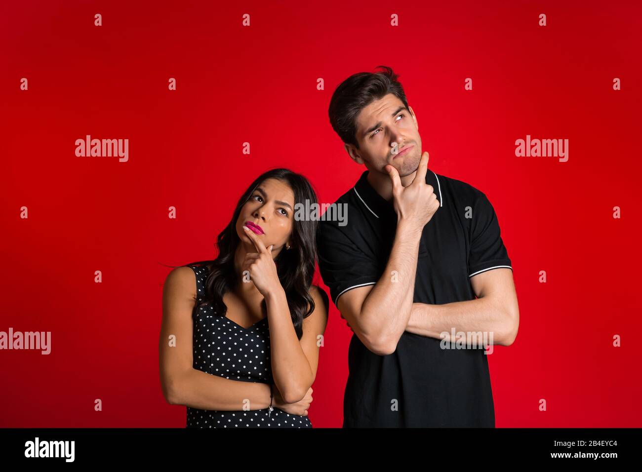 Portrait of young thinking pondering couple on red studio background ...