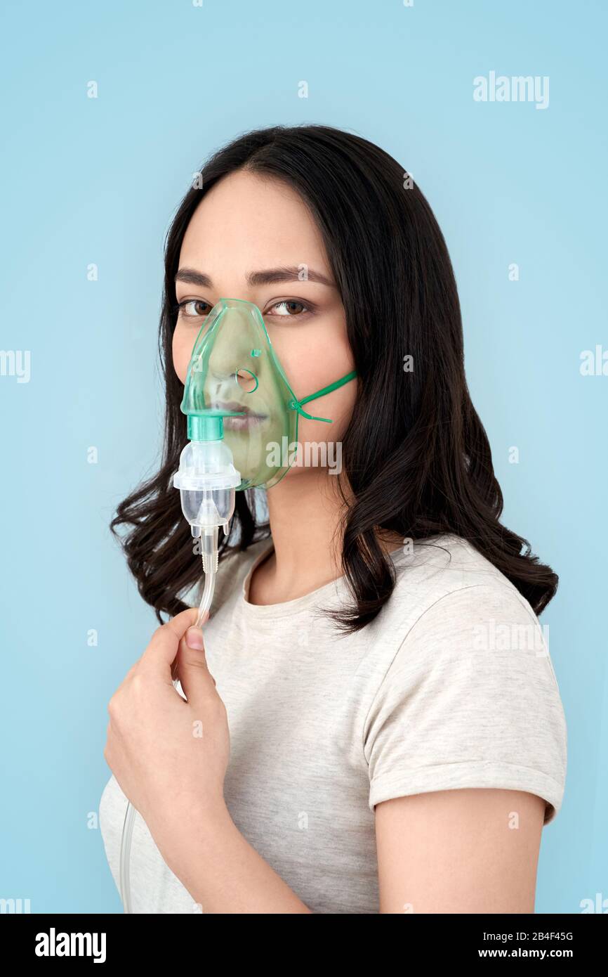 Young chinese woman wearing oxygen mask standing isolated on grey ...