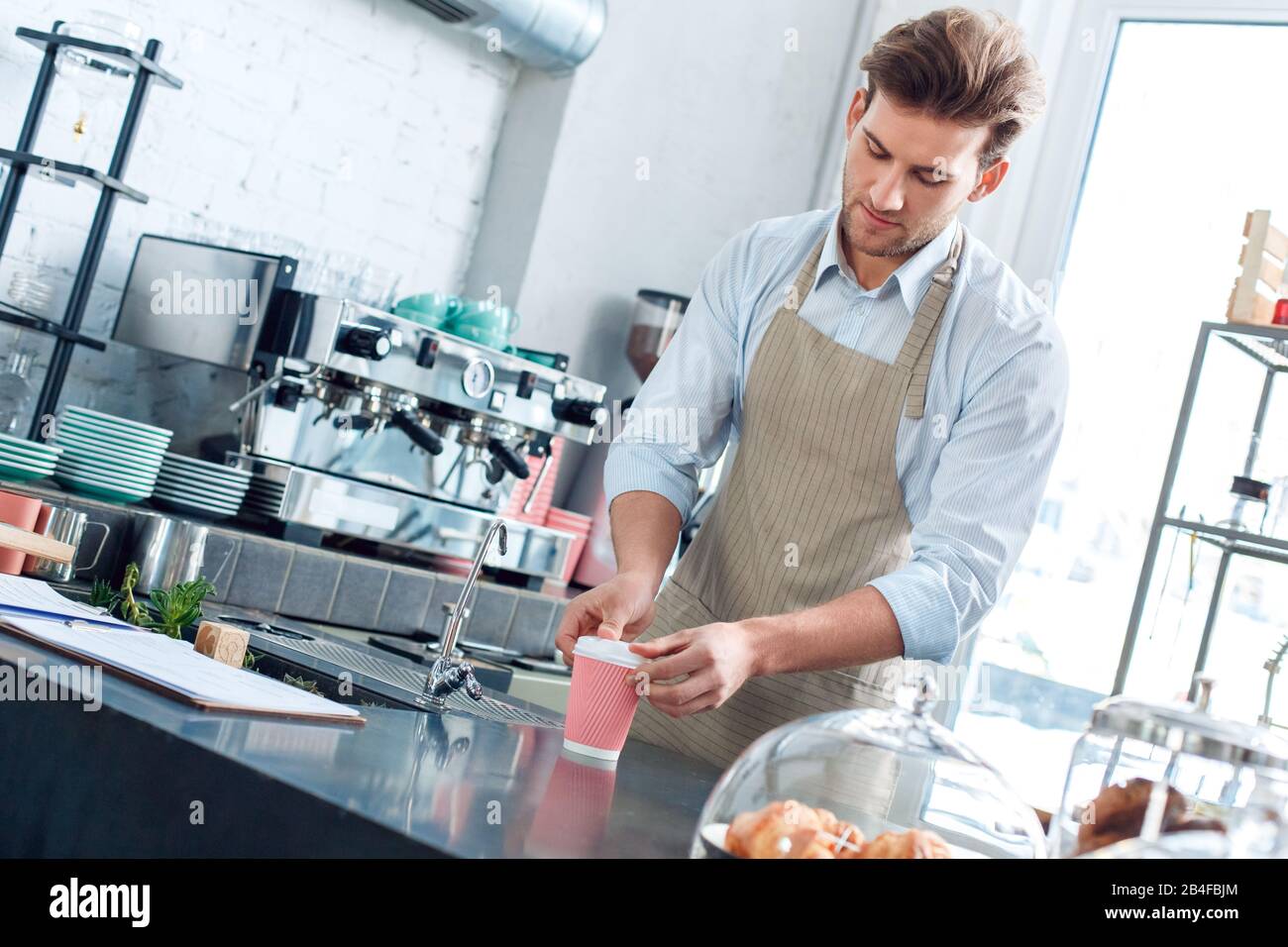 Concentrated young adult barista wearing in uniform, working in ...