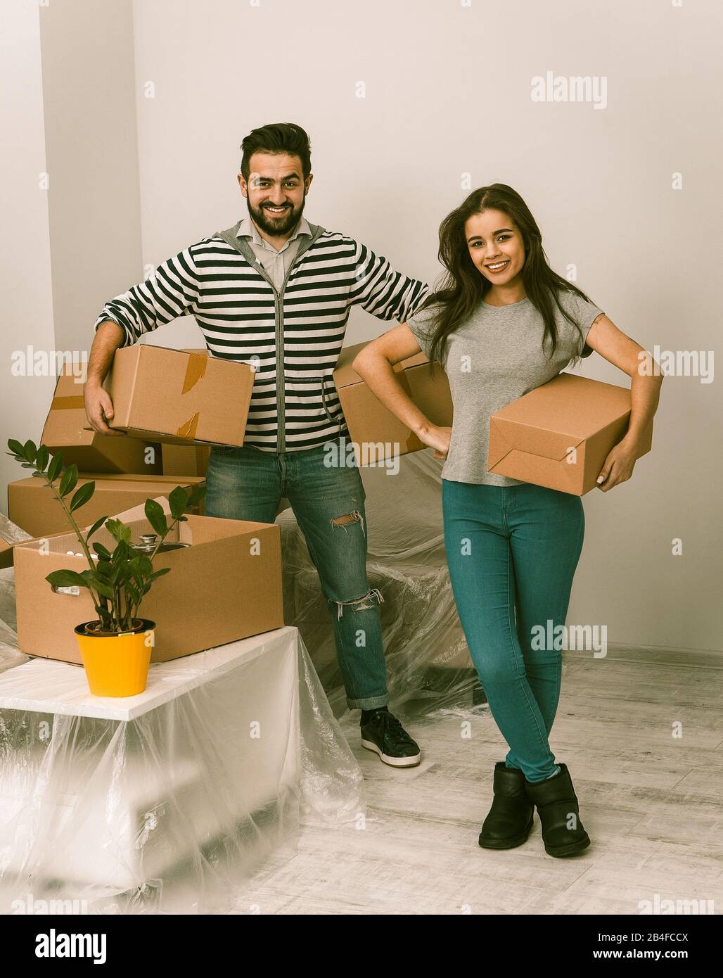 Excited young couple moving home standing close together with cardboard ...