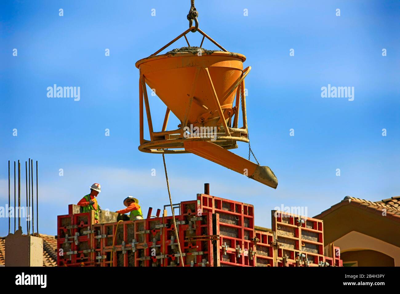A yellow wet cement bucket being hoisted into a construction site area ...