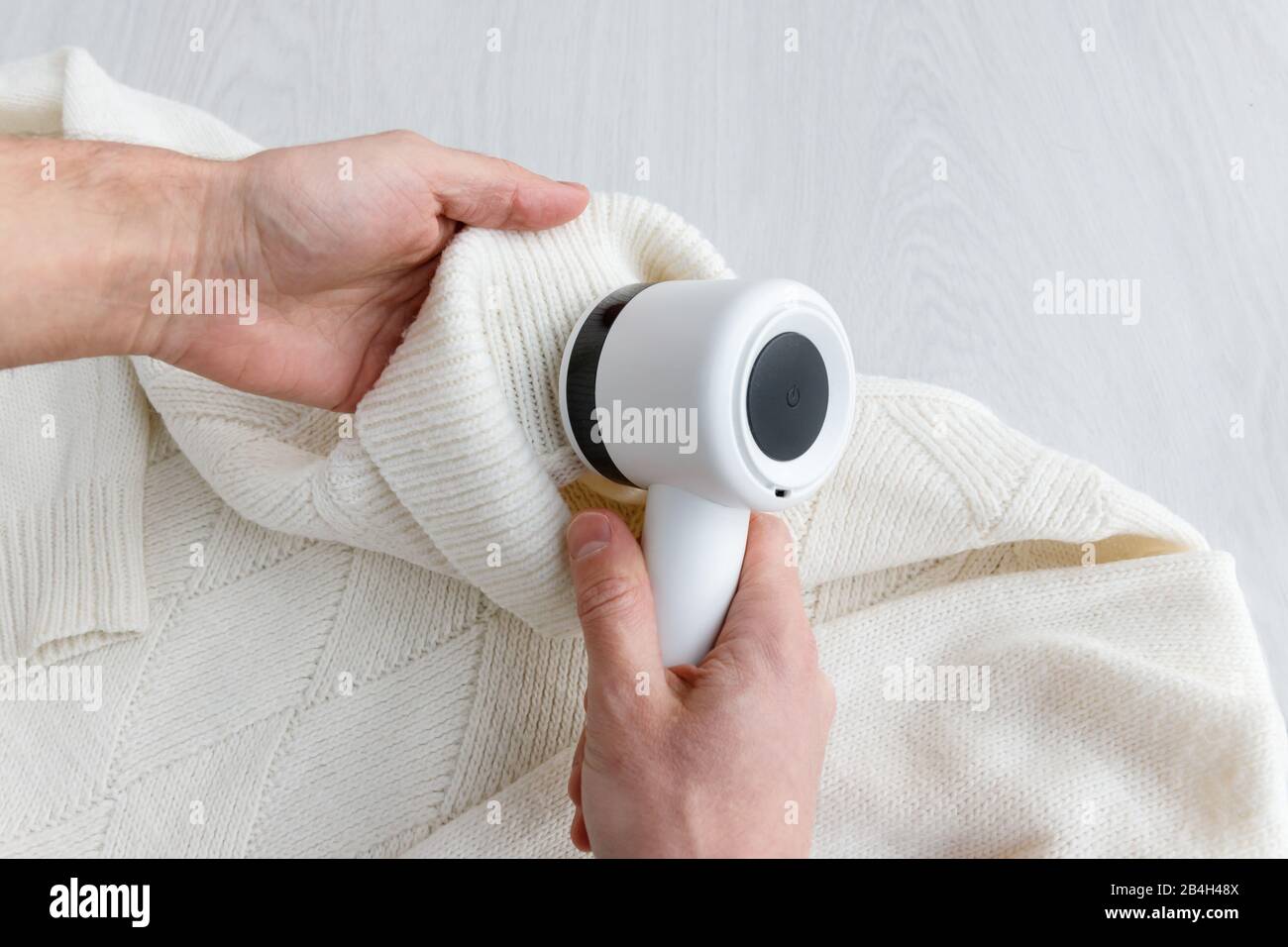 Man's hand holding a lint remover from a white acrylic or wool sweater ...