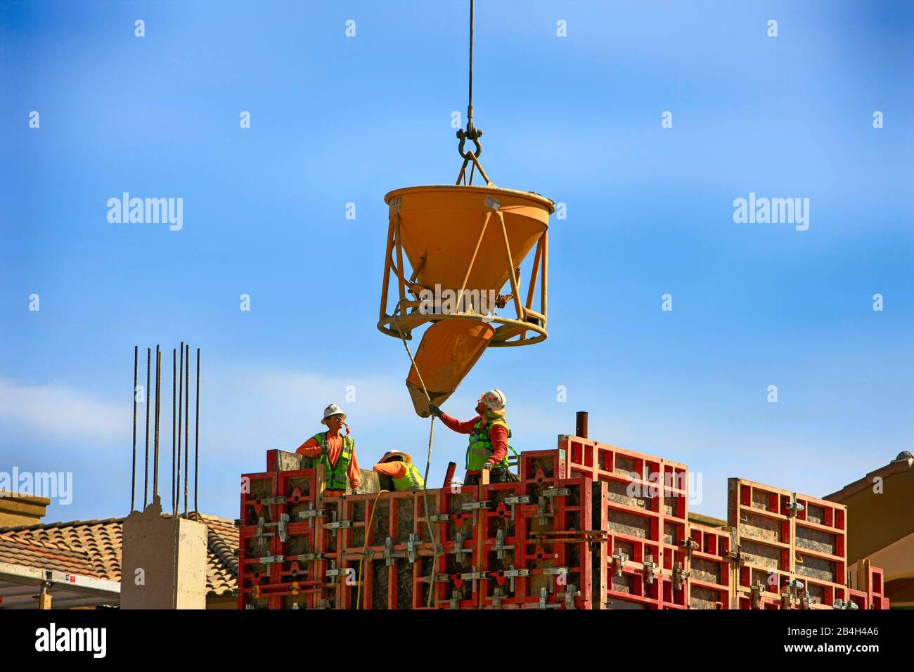 A yellow wet cement bucket being hoisted into a construction site area ...