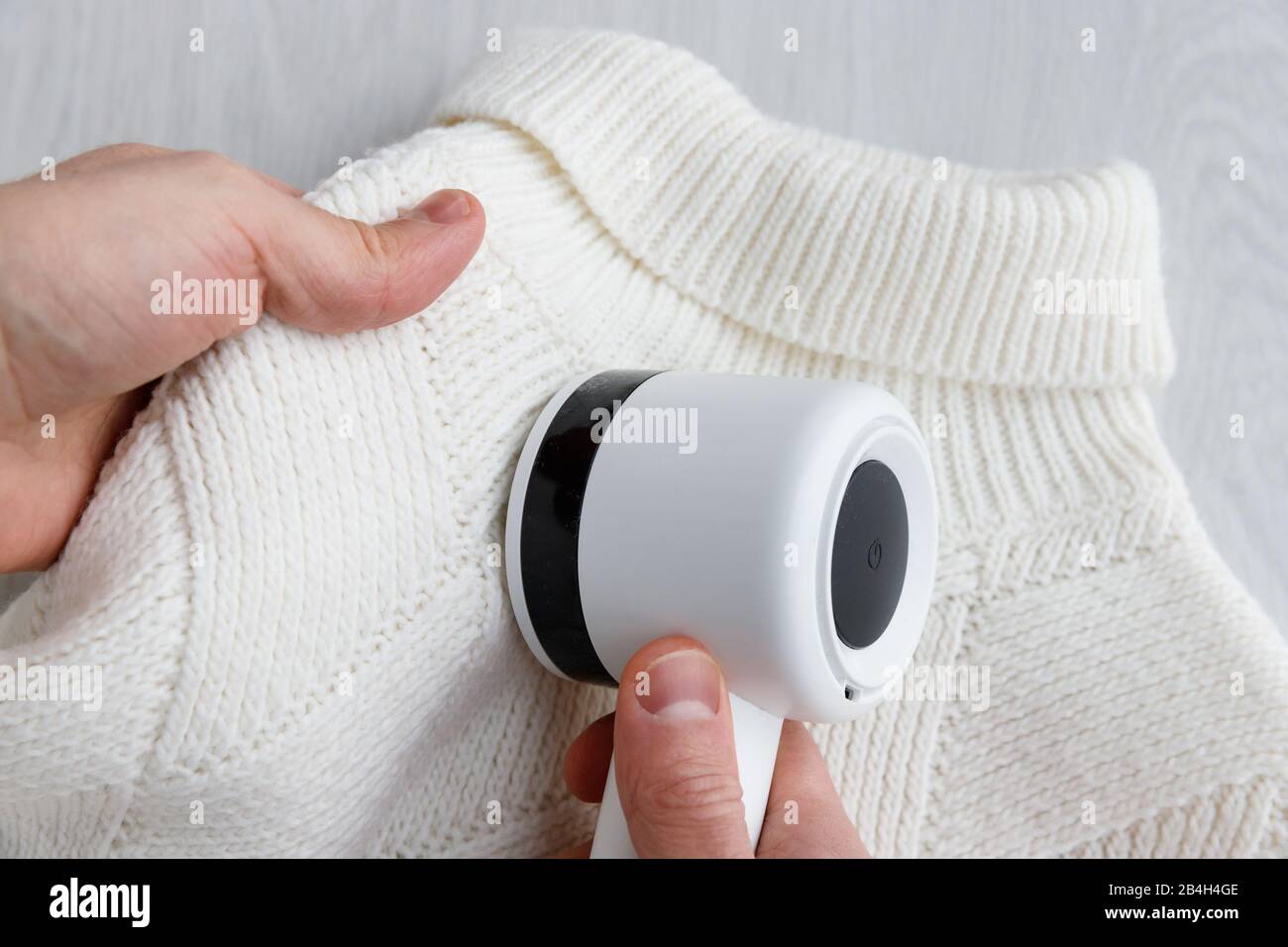 Man's hand holding a lint remover from a white acrylic or wool sweater ...