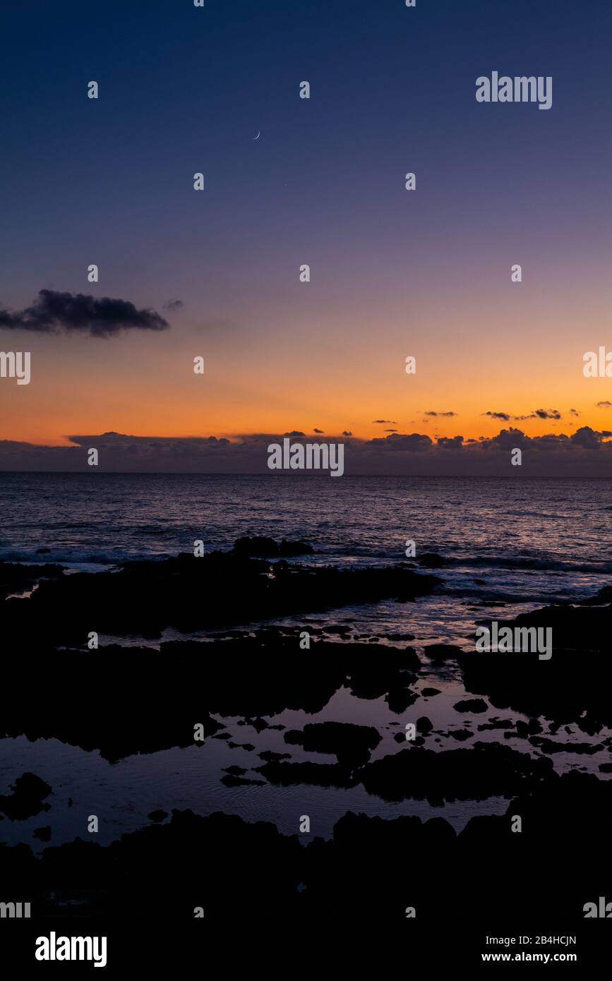 Crescent Moon in colorful sunset sky above tide pools at edge of ocean ...