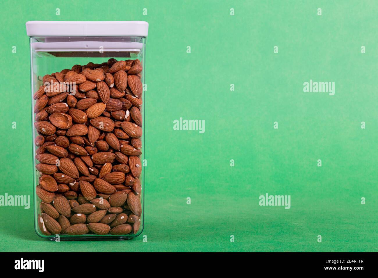 Almonds inside a transparent plastic container with a green background ...