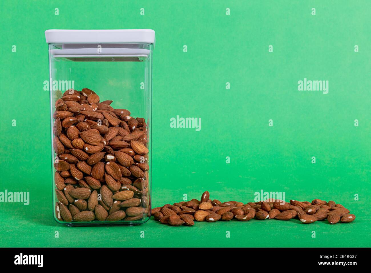Almonds inside a transparent plastic container with a green background ...