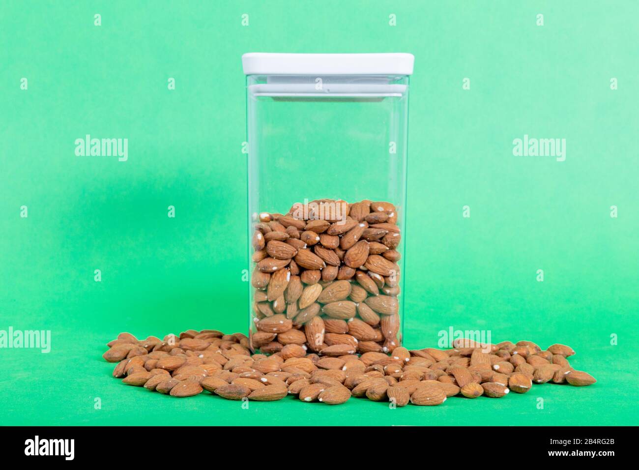 Almonds outside and inside a transparent plastic container with a green ...
