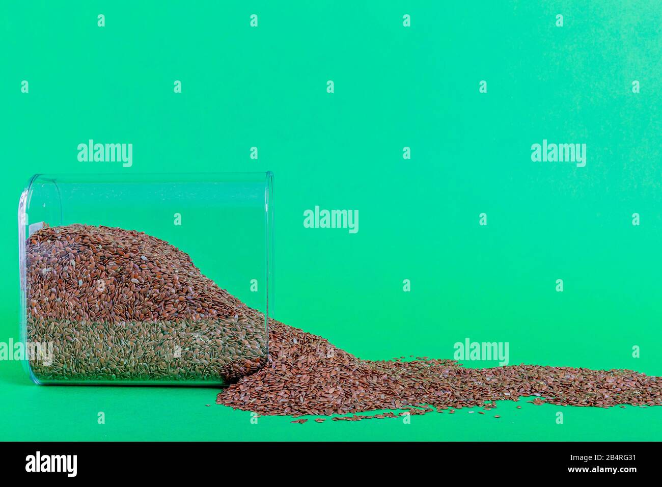 Plastic container tilted on a surface with brown flax seeds watered ...