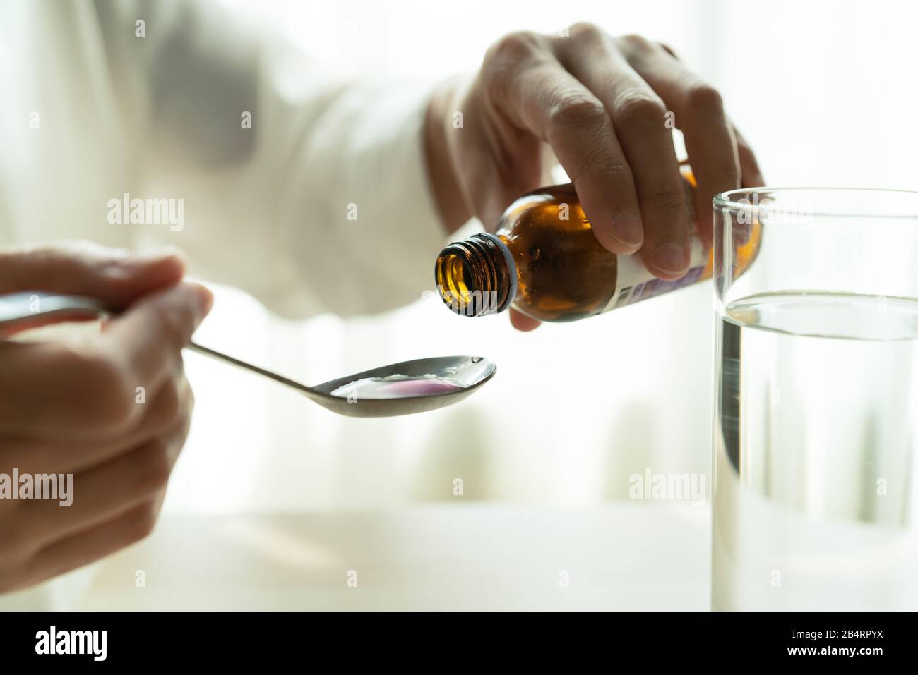 Woman hand pouring medication or cough syrup from bottle to spoon ...