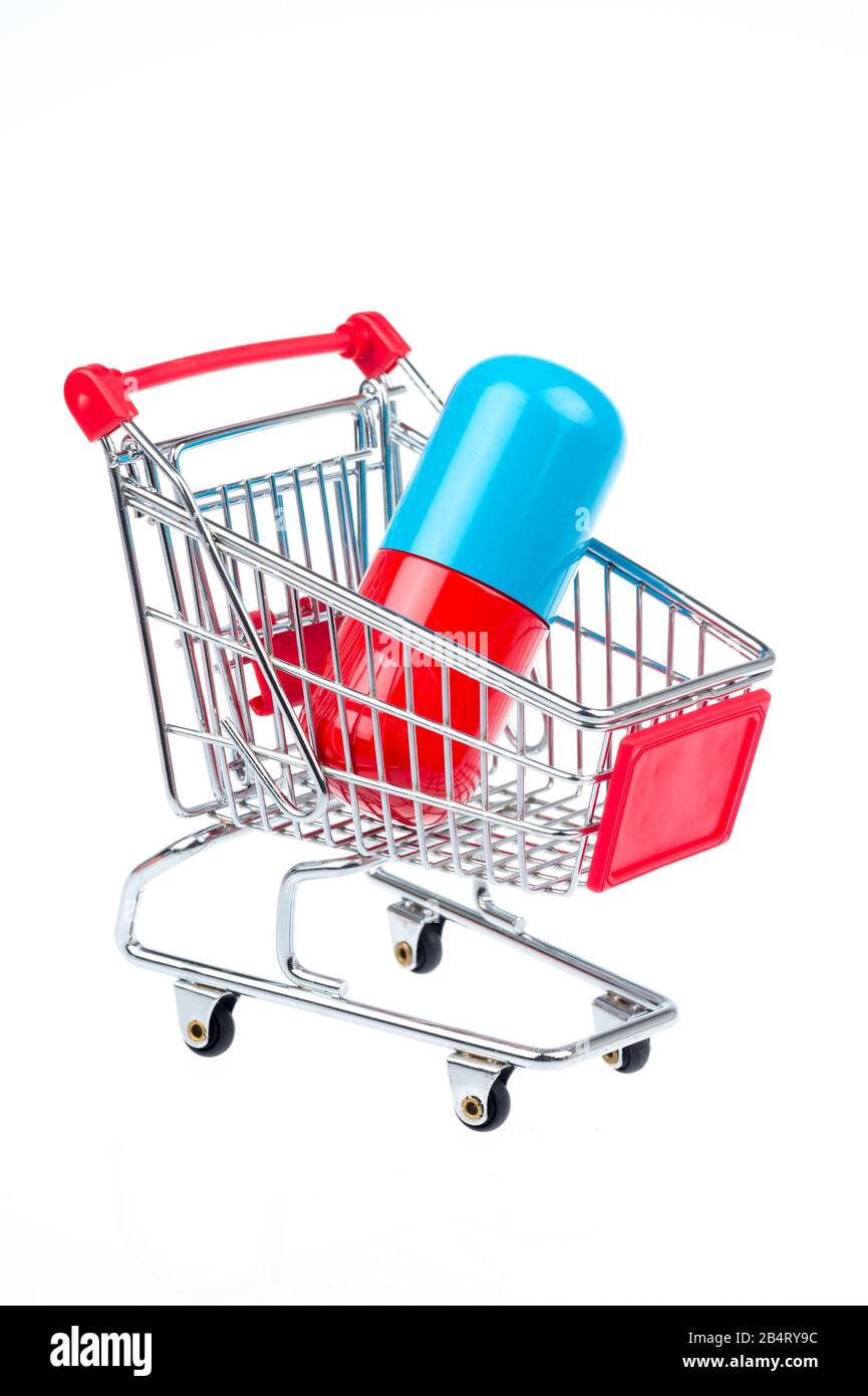 Miniature shopping cart carrying large pill capsule on white background ...