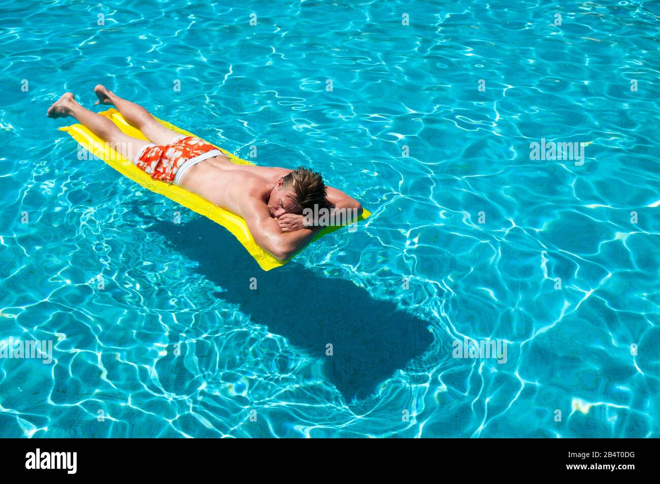 Unrecognizable man in colorful swim shorts floating on an inflatable ...