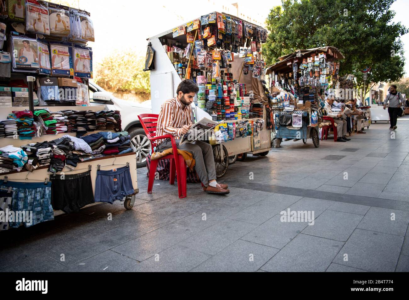Iraq, Iraqi Kurdistan, Arbil, Erbil. A man is reading on a red chair in ...