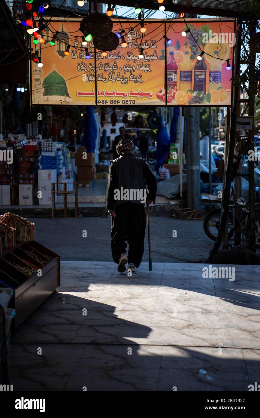 Iraq, Iraqi Kurdistan, Arbil, Erbil. A man walks with a cane under an ...