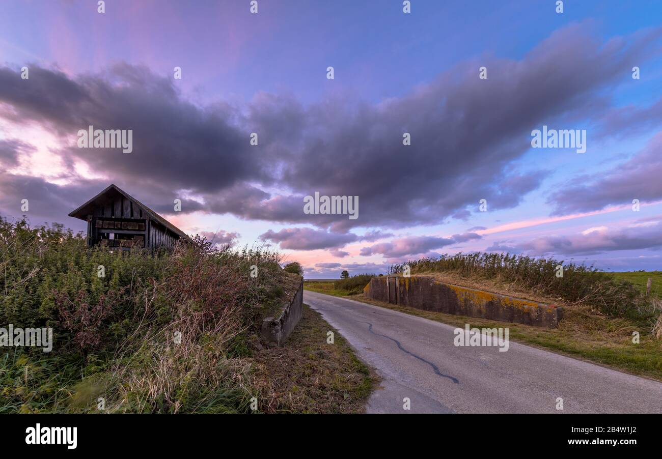 Road passage through dike at sunset under beautiful clouded sky ...