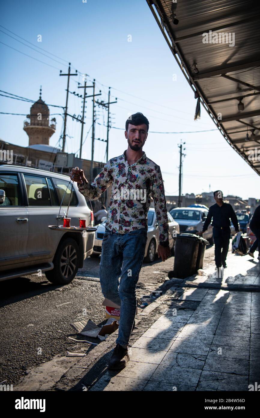 Iraq, Iraqi Kurdistan, Arbil, Erbil. A man is walking with two cups of ...