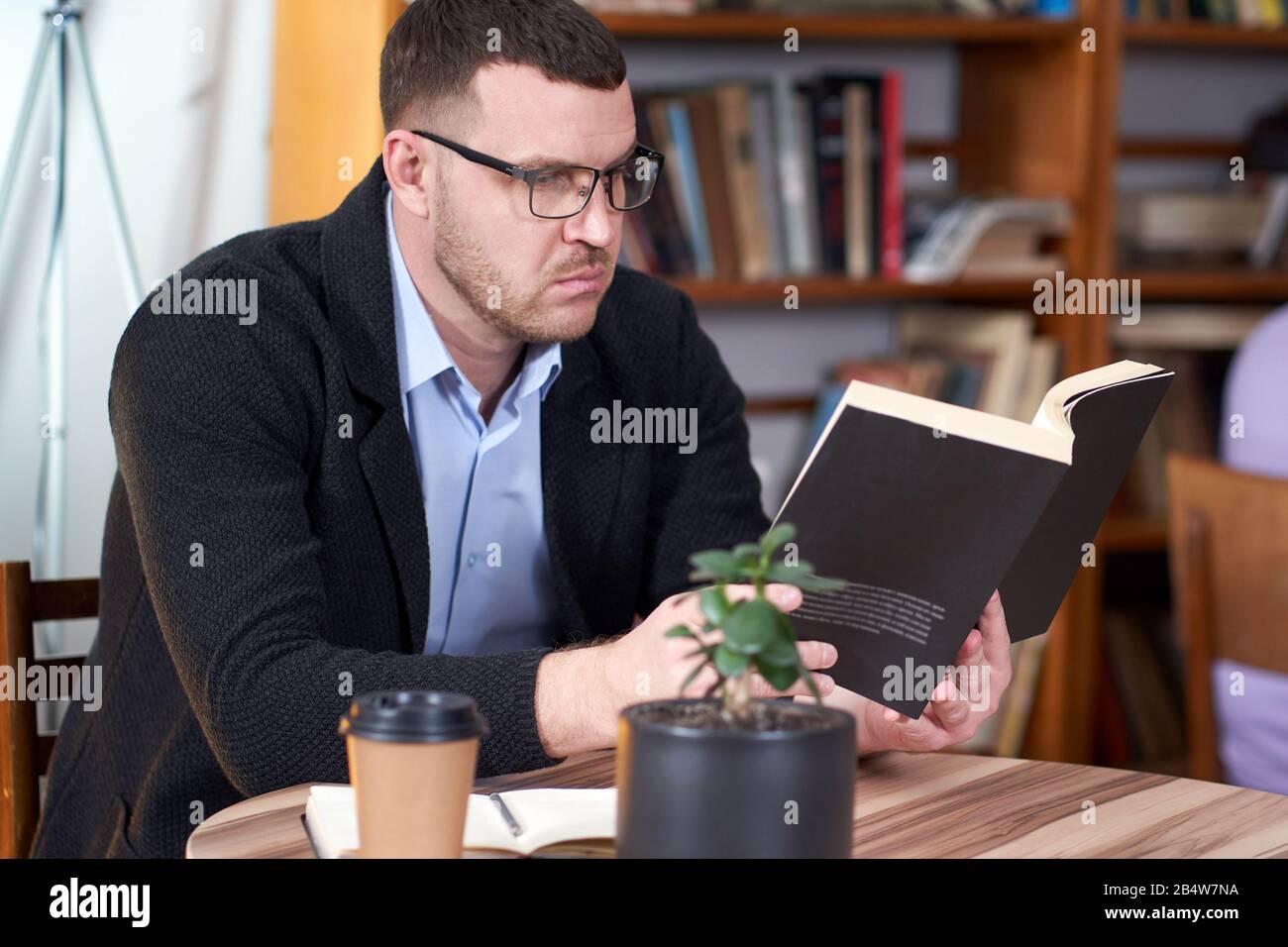 Man reading book and drinking coffee in a cafe with many books on a ...