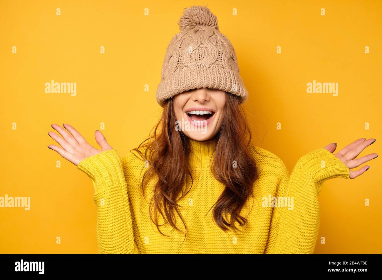 A girl in a yellow sweater stands on a yellow background with a cap ...