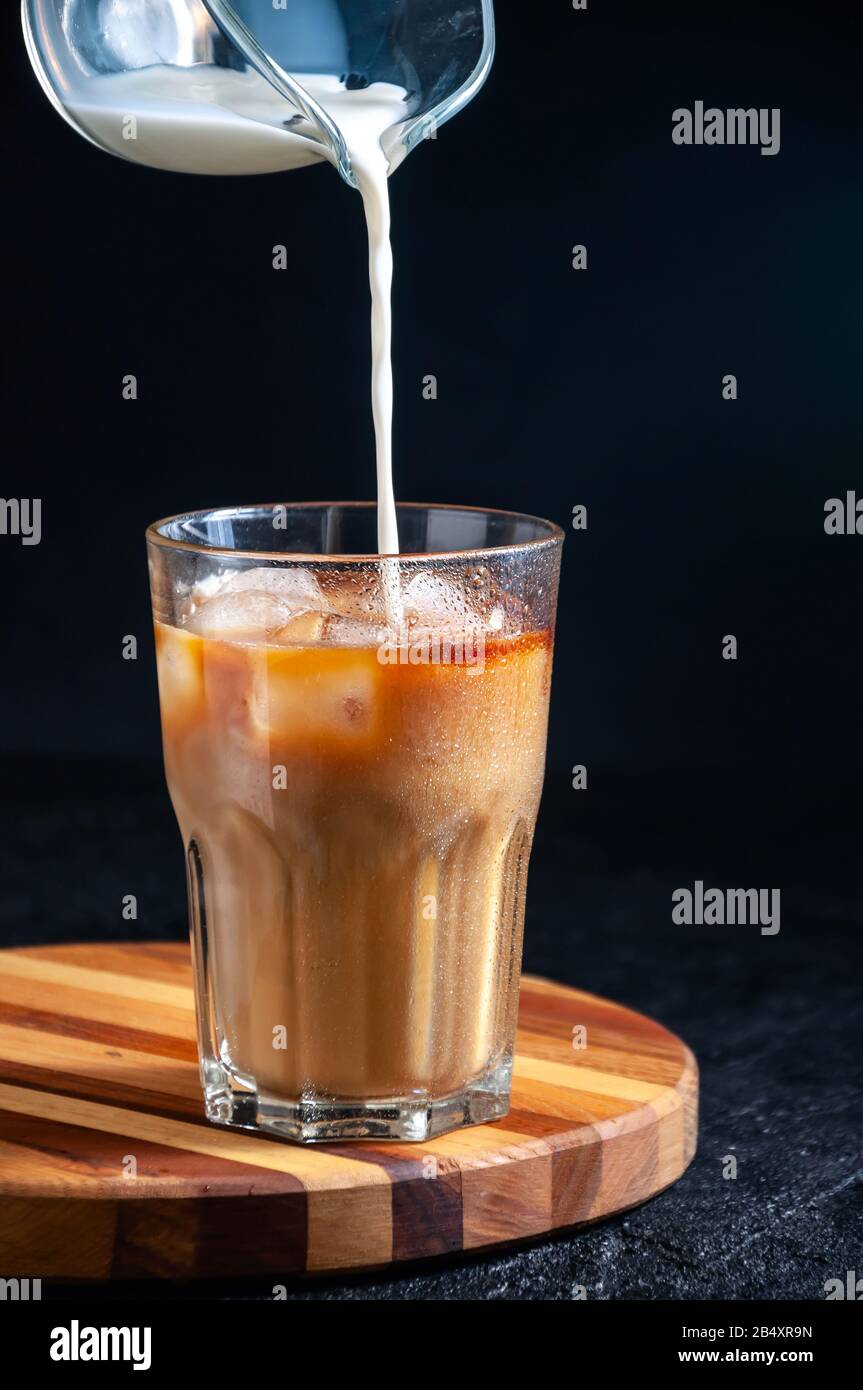 Milk Being Poured into Iced Coffee in Tall Glass on Dark Background. Concept Refreshing Summer ...