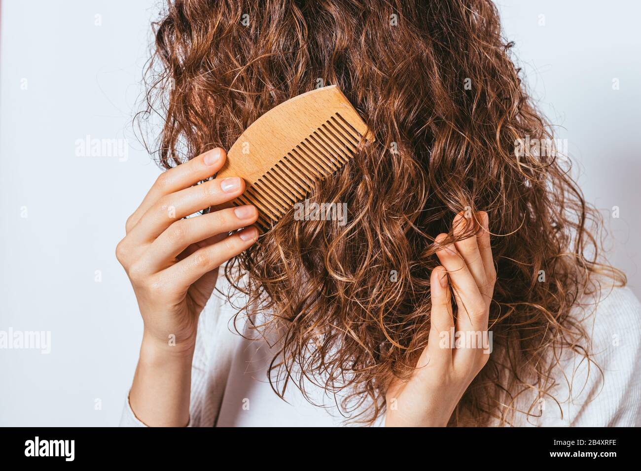 Close-up young woman combing her curly hair with wooden comb standing ...