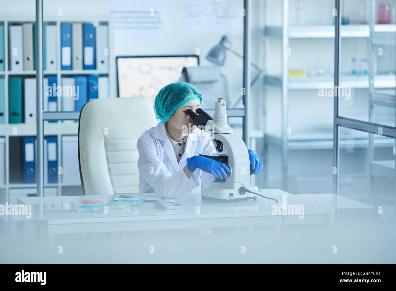 Horizontal portrait of young Asian female scientist sitting alone at ...