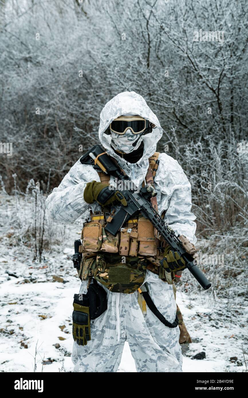 Military man in white camouflage uniform with machinegun. Soldier in the winter forest territory ...