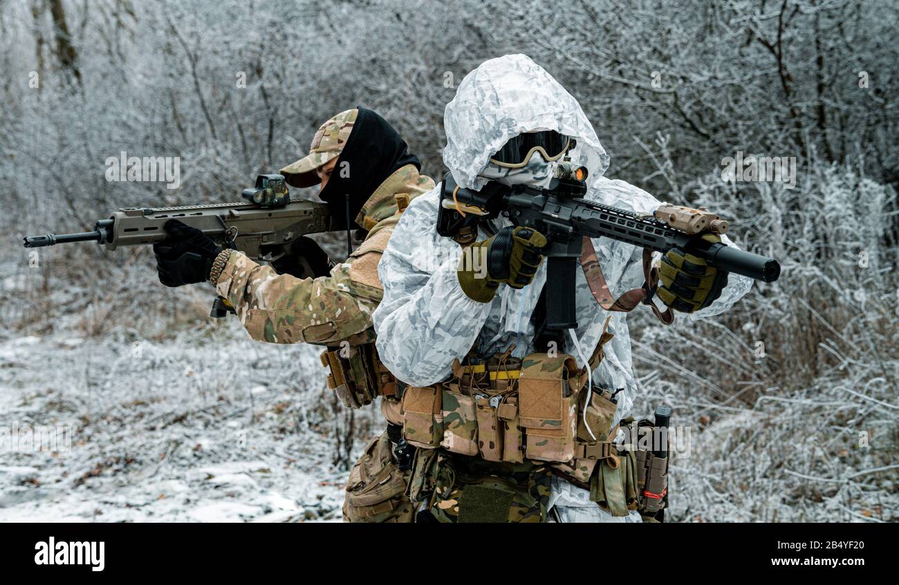 Two men in camouflage white, green uniform with machineguns back to ...