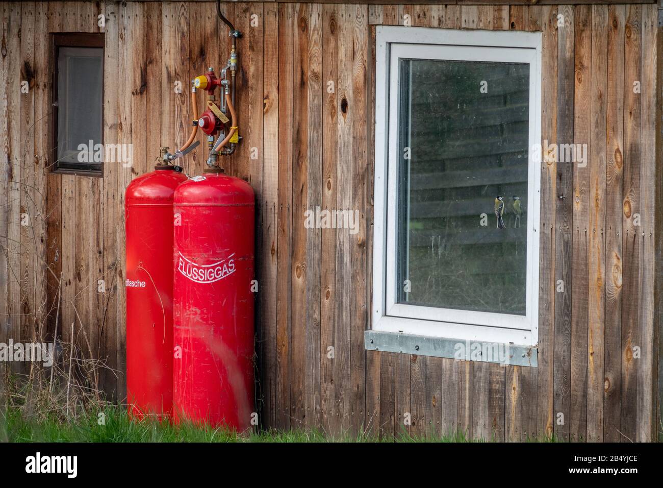 on the outside wall of a small wooden house are two big red gas bottles ...