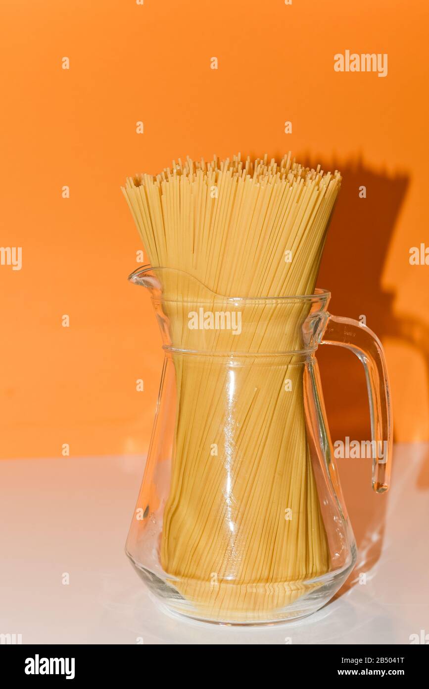 Yellow spaghetti in a glass jug on an orange background, shooting with ...