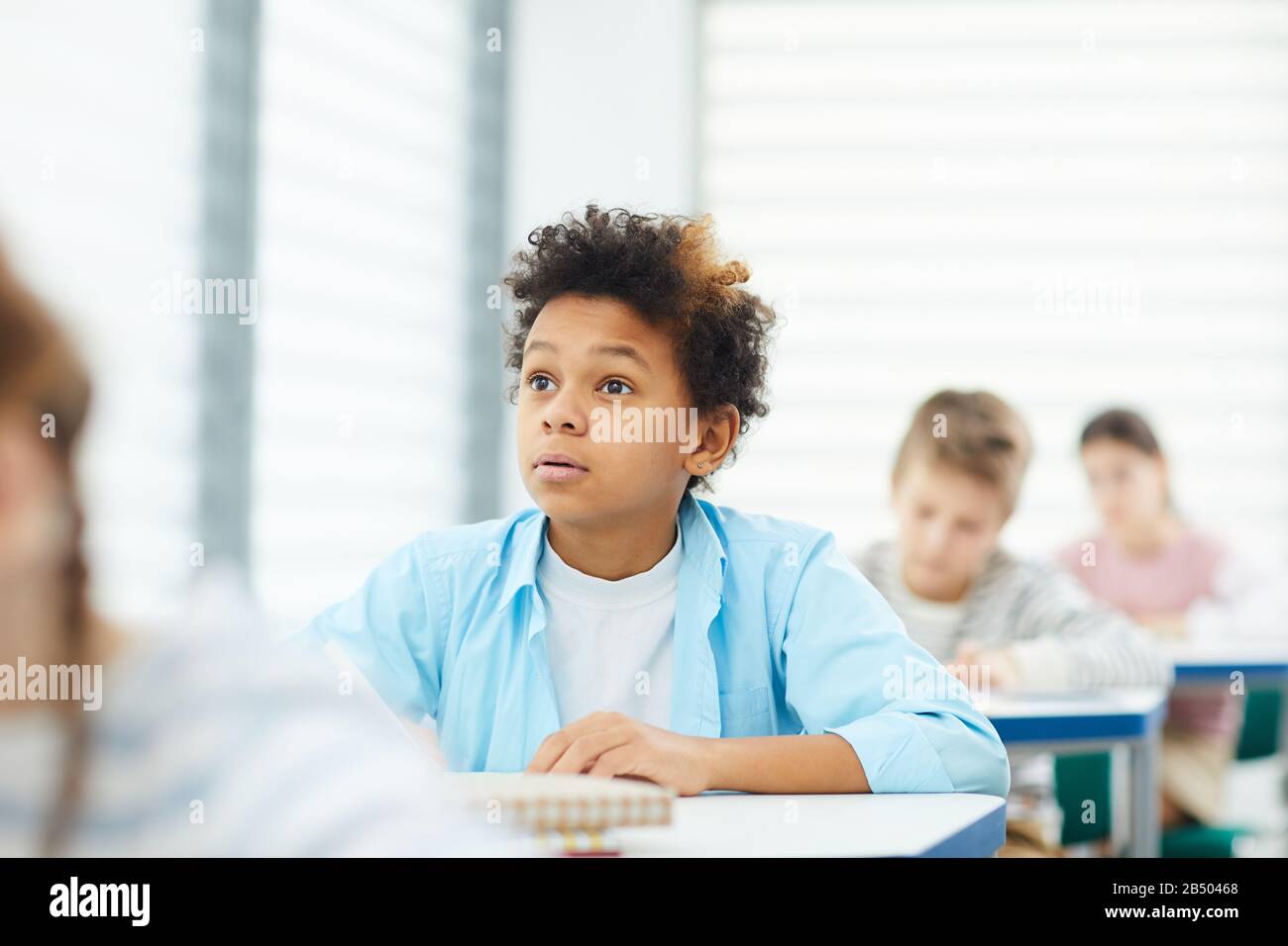 Curious teen boy with eyes wide open sitting at school desk listening ...