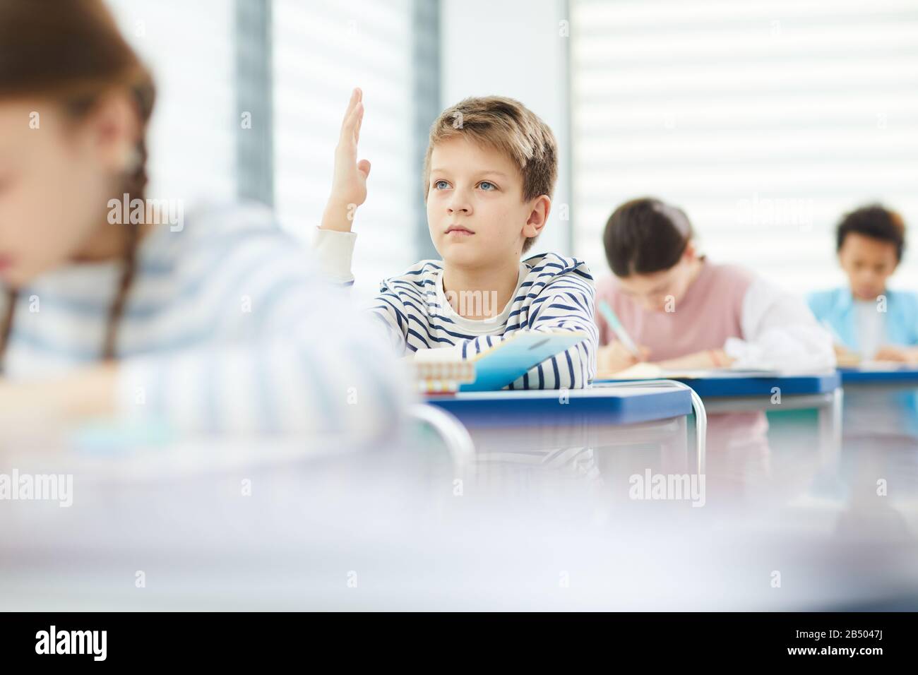 Horizontal portrai of modern primary school male student sitting at ...