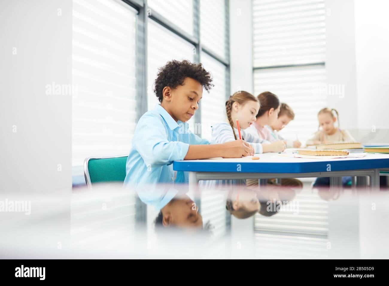 Pensive children wearing casual outfits sitting at school desk in ...