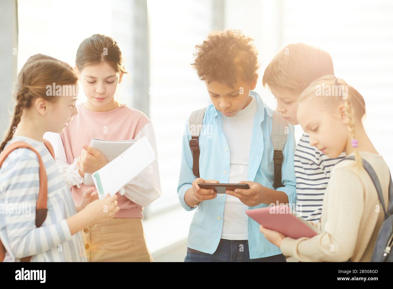 Group of five middle schoolers standing together in corridor checking ...