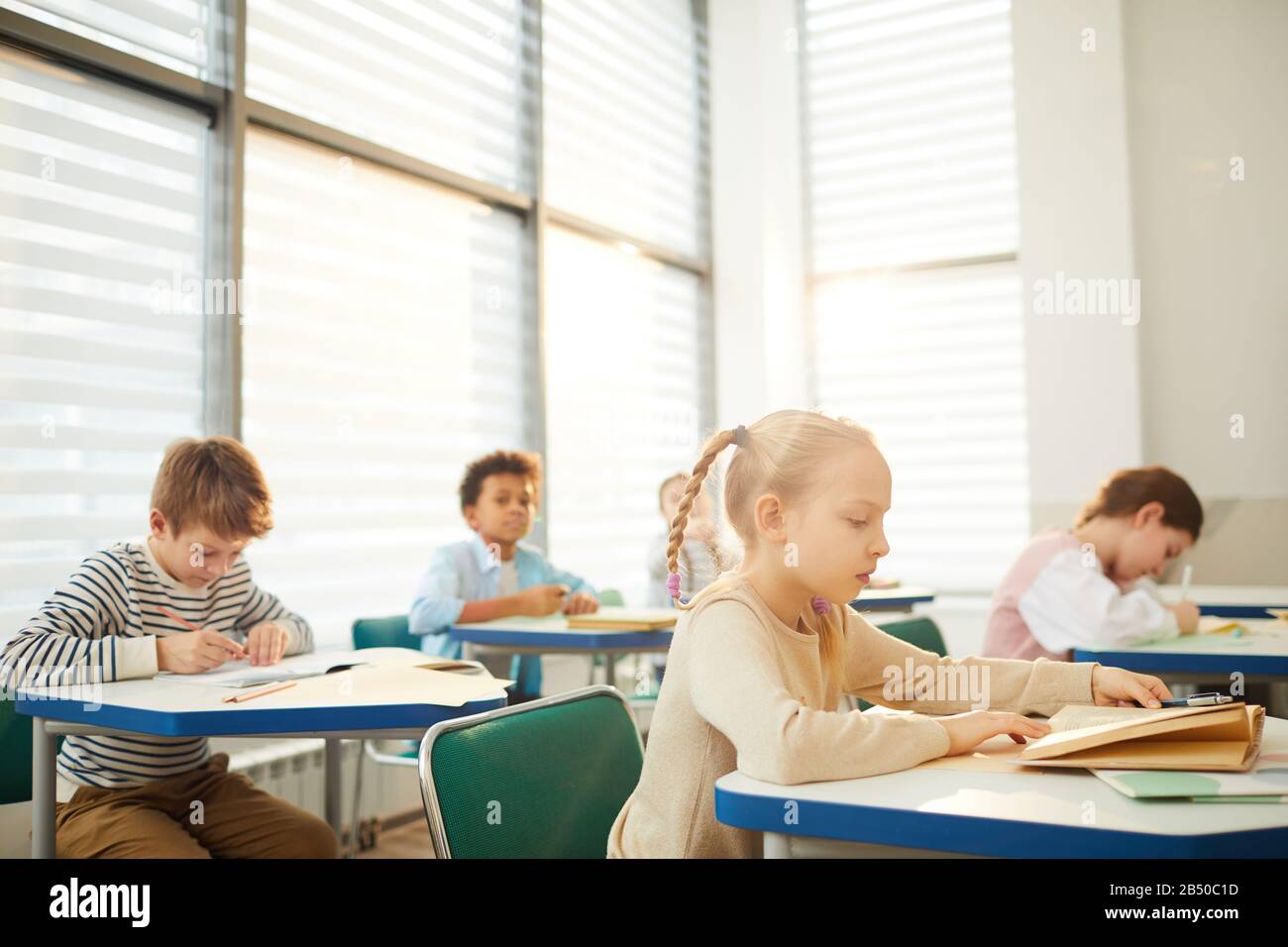 Horizontal shot of young middle school students sitting at desks in ...