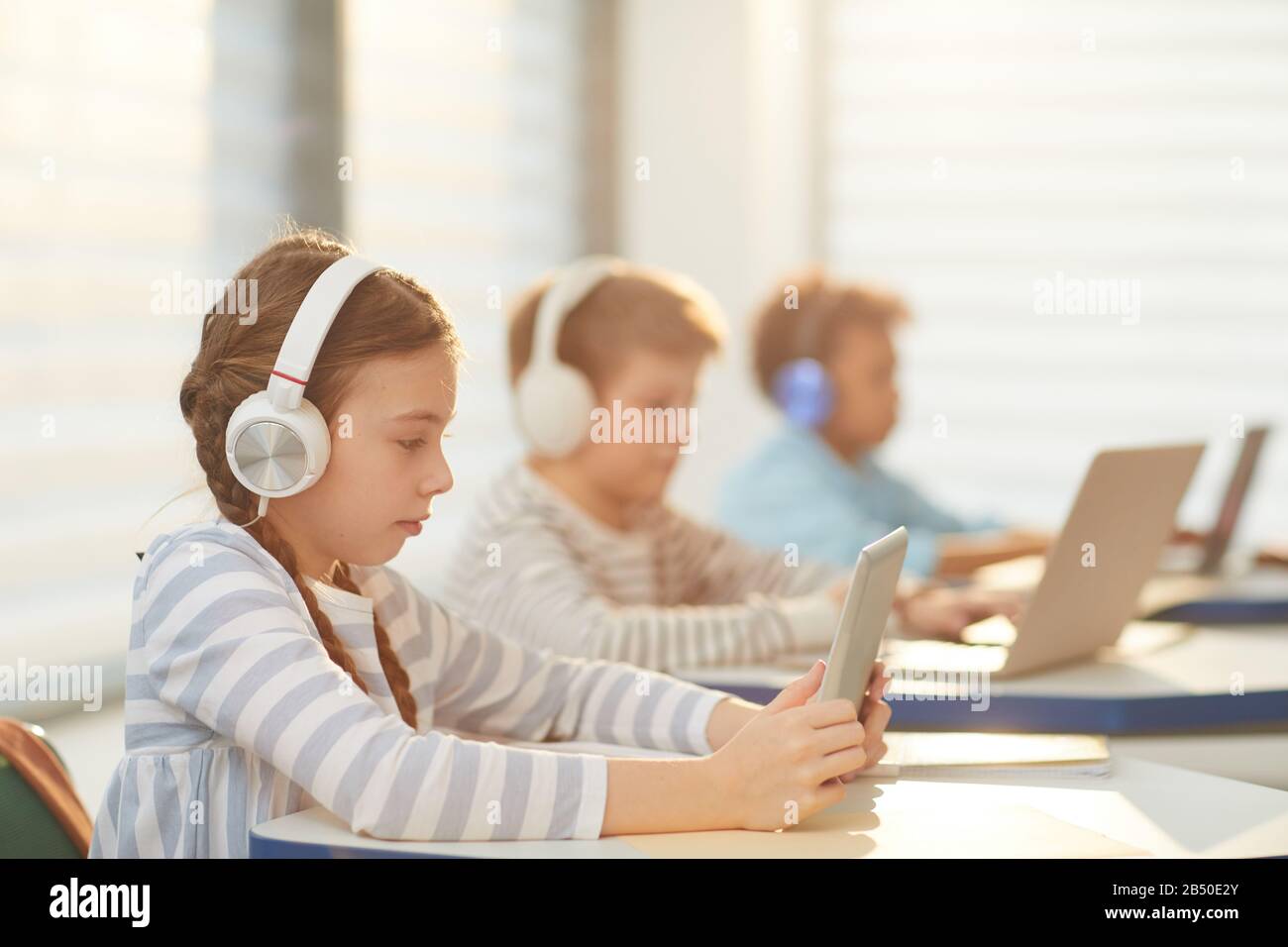 Middle school students sitting in classroom using modern headphones and ...