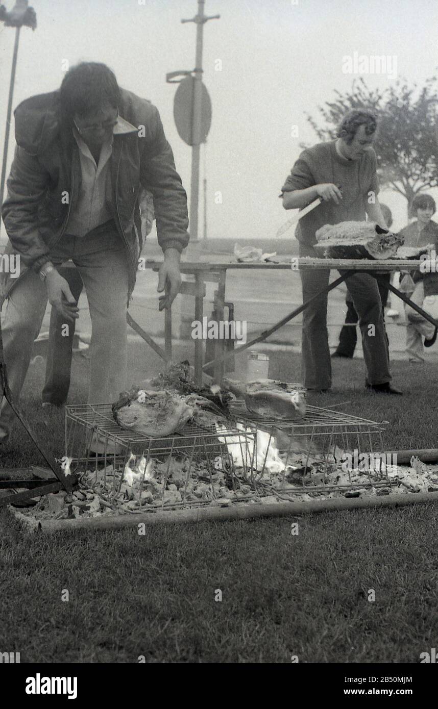 1970s, historical, large pieces of meat being cooked on a DIY barbeque ...