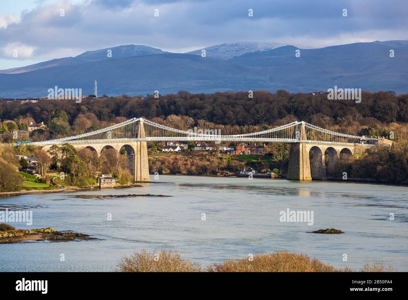 The Menai Bridge across the Menai Strait with snow covered Snowdonia ...
