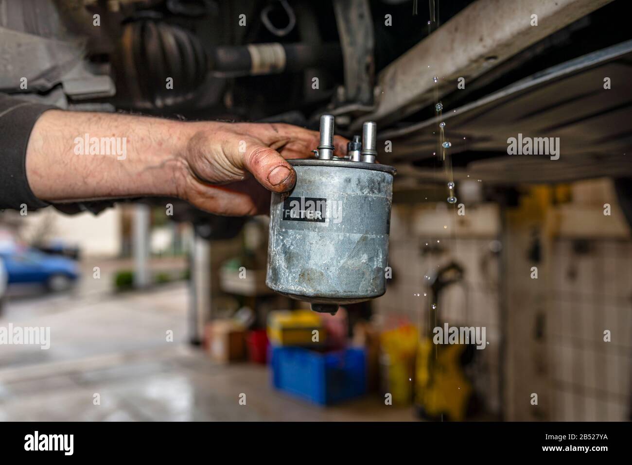 Car mechanic holding a used fuel filter in the background, car on a ...