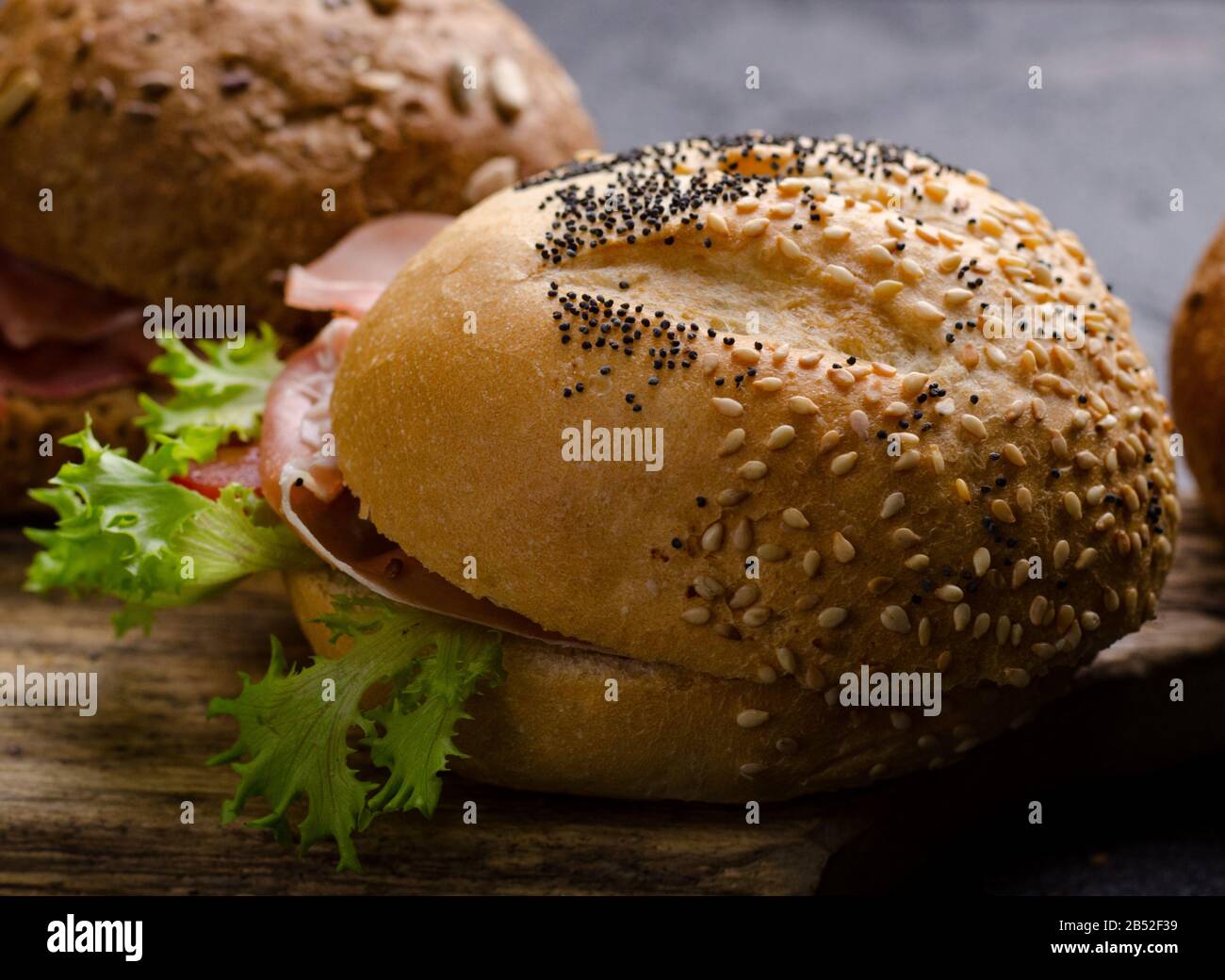 Delicious crispy burger bun with sliced ham on a vintage wooden cutting ...