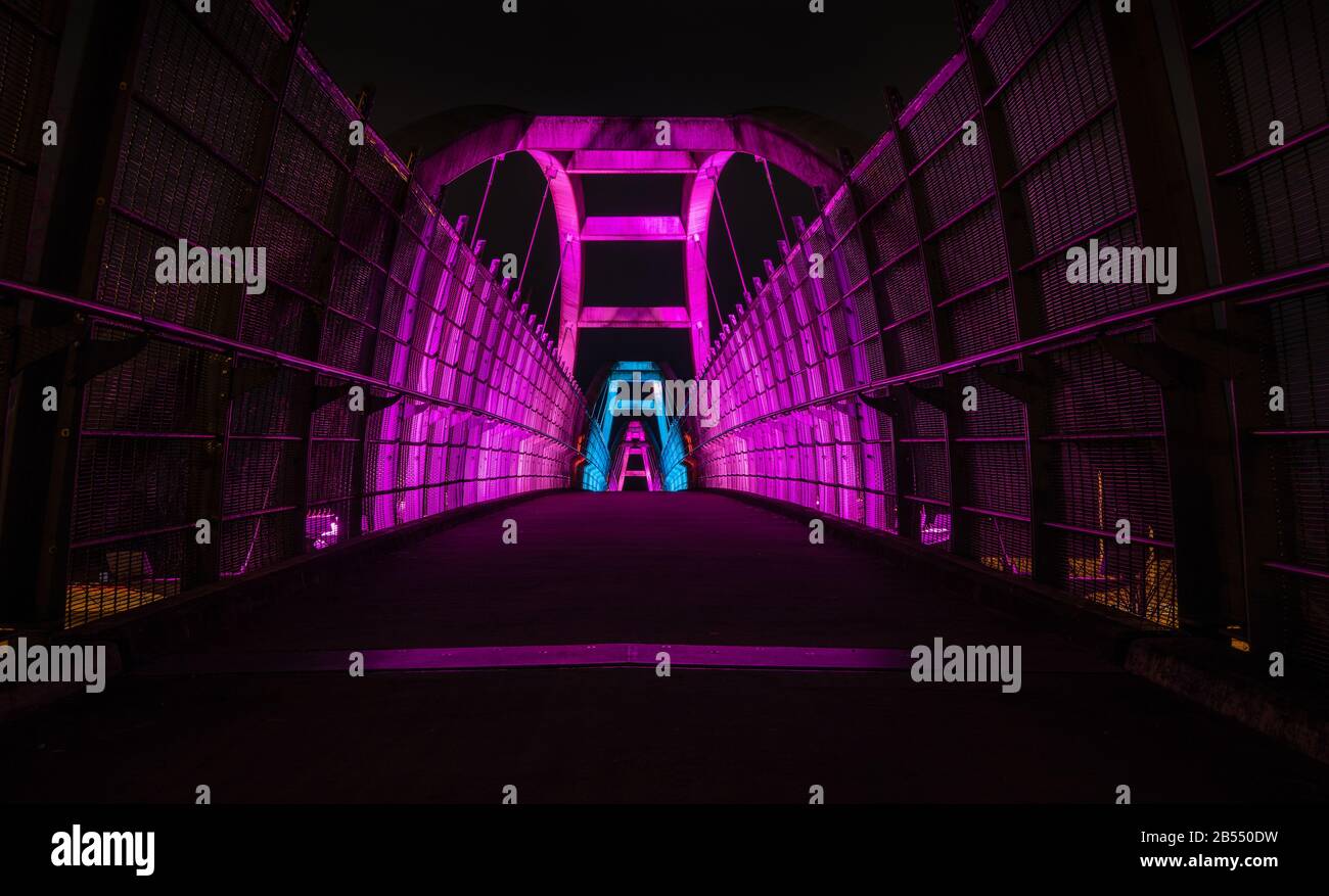 Bright purple leds illuminate pedestrian walkway over highway at night ...