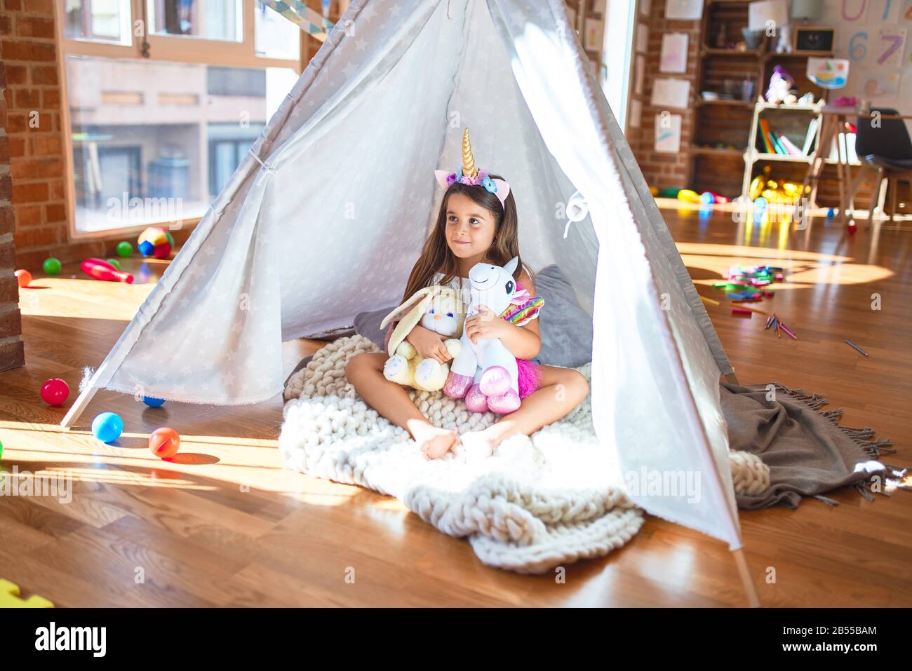 Adorable toddler sitting on the floor inside tipi around lots of toys ...
