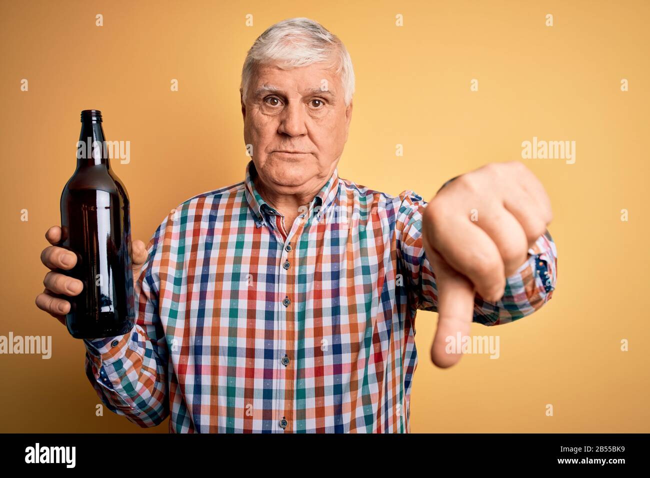 Senior handsome hoary man drinking bottle of beer standing over ...