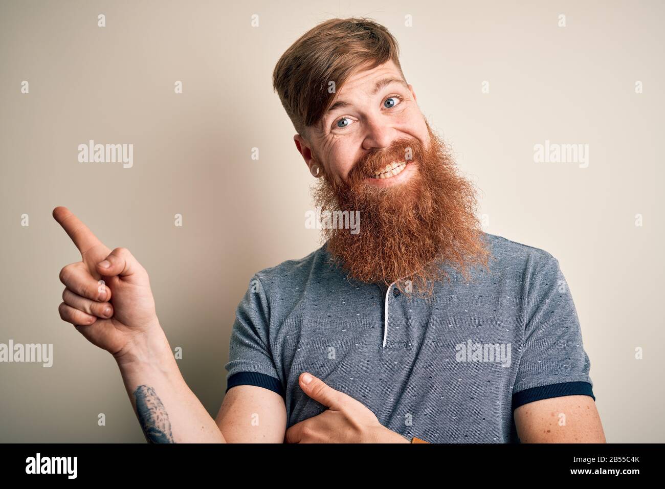 Handsome Irish redhead man with beard and arm tattoo standing over ...