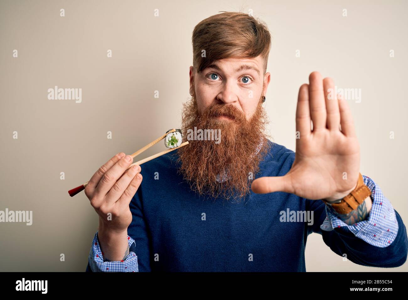 Redhead Irish Man With Beard Eating Green Maki Sushi Using Chopsticks Over Yellow Background