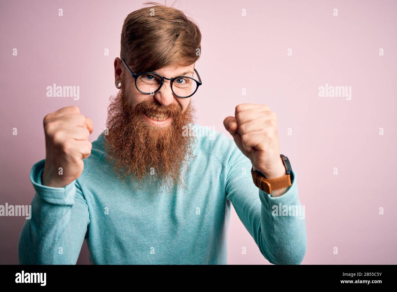 Handsome Irish redhead man with beard wearing glasses over pink ...